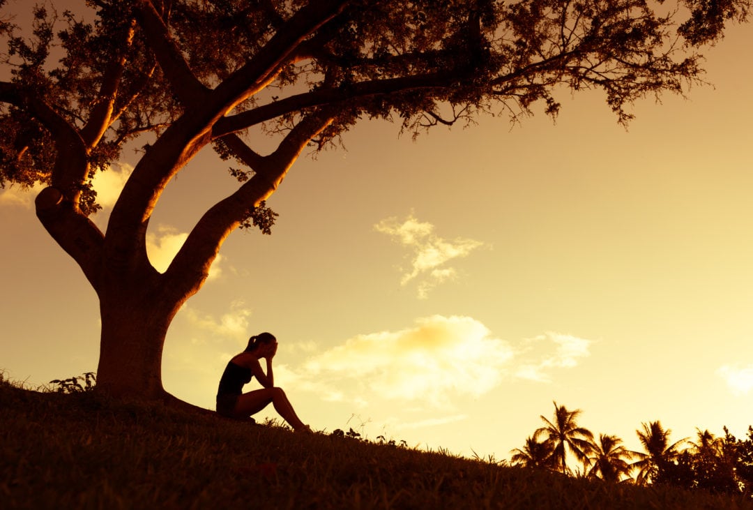 Sad young woman sitting outdoors under a tree. | Strive For More